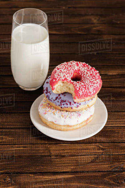 Close up of glass of milk with donuts on plate on wooden background ...