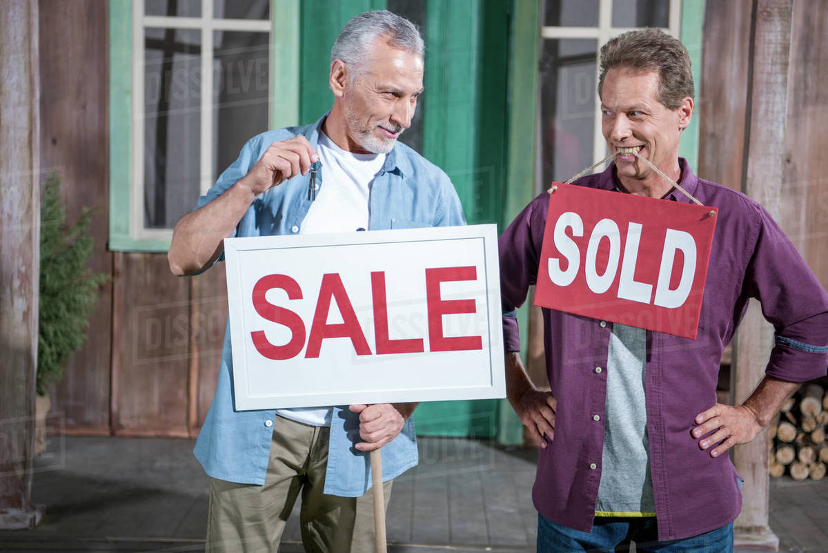 Senior man holding sale sign while another man holding sold sing, house ...