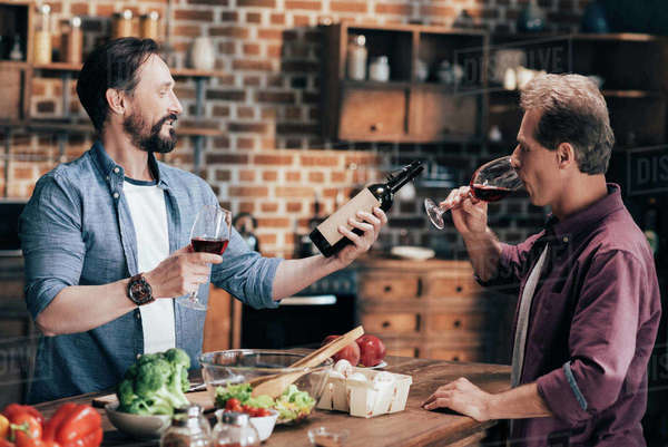 Two middle aged men drinking wine and looking at wine bottle while ...