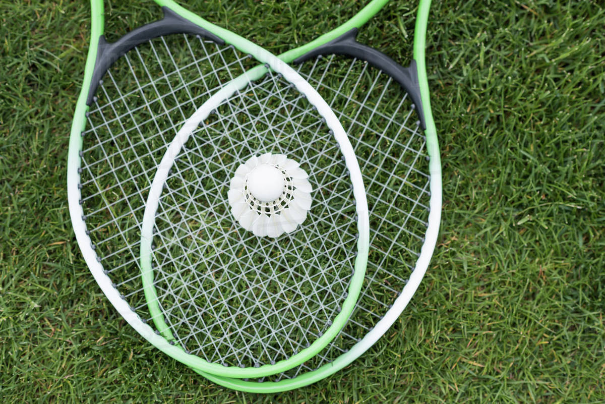 Top view of shuttlecock on badminton rackets lying on green grass ...