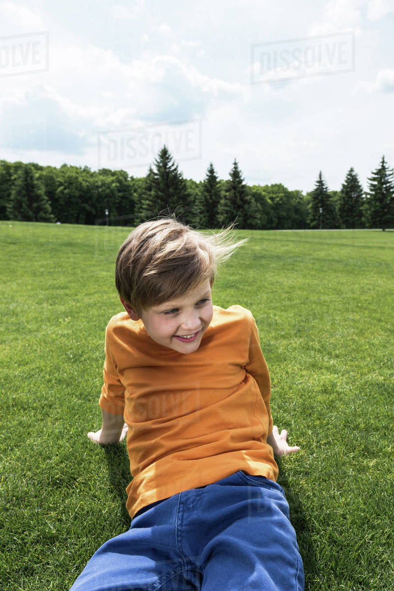 Portrait of cheerful boy looking away while resting on green lawn ...