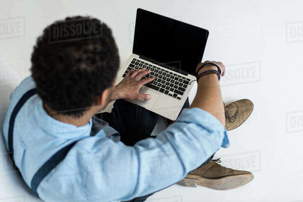 High angle view of young man sitting and using laptop with blank screen ...