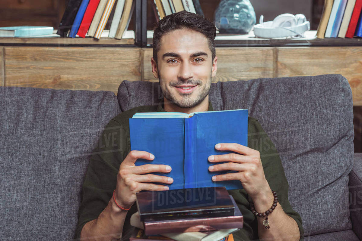 Handsome male student reading books and smiling at camera - Royalty ...