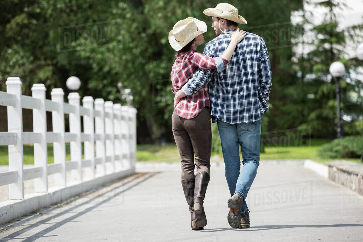Back view of cowboy with his girlfriend walking on pathway in park at ...