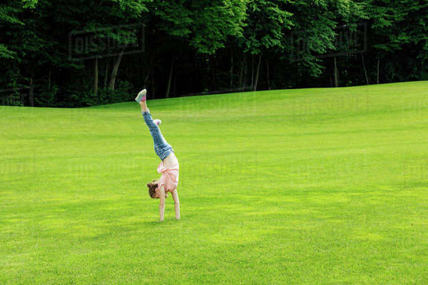 Full length view of cute little girl performing handstand on green ...
