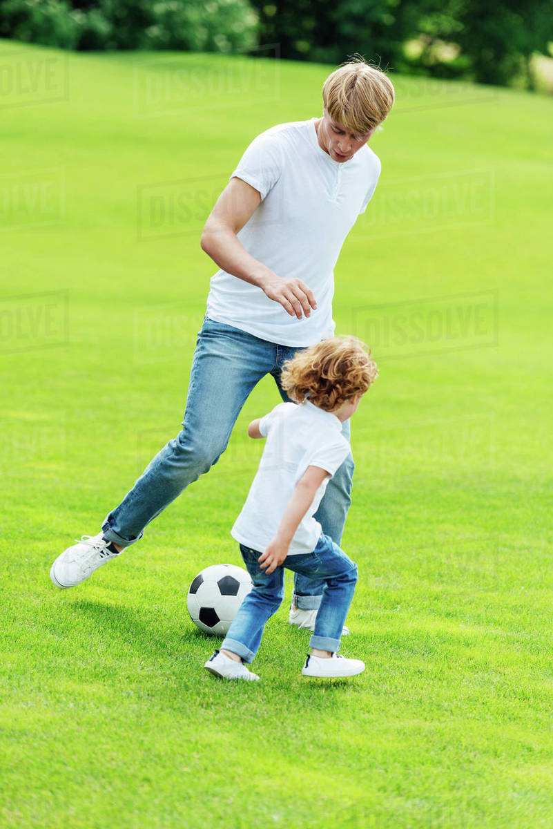 Happy father and son playing soccer on green grass in park - Royalty ...