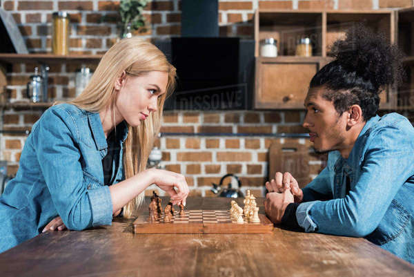 Side view of multiethnic young couple playing chess together in kitchen ...