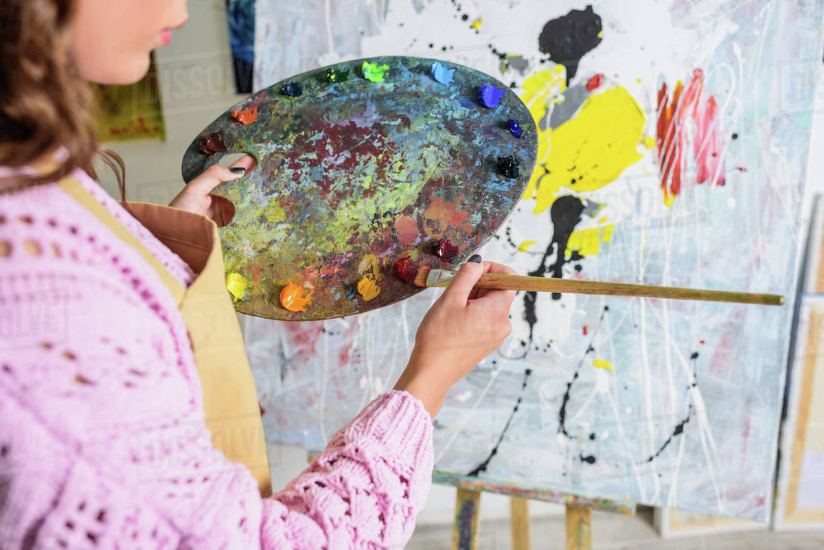 Cropped image of female artist taking paint from palette in workshop ...