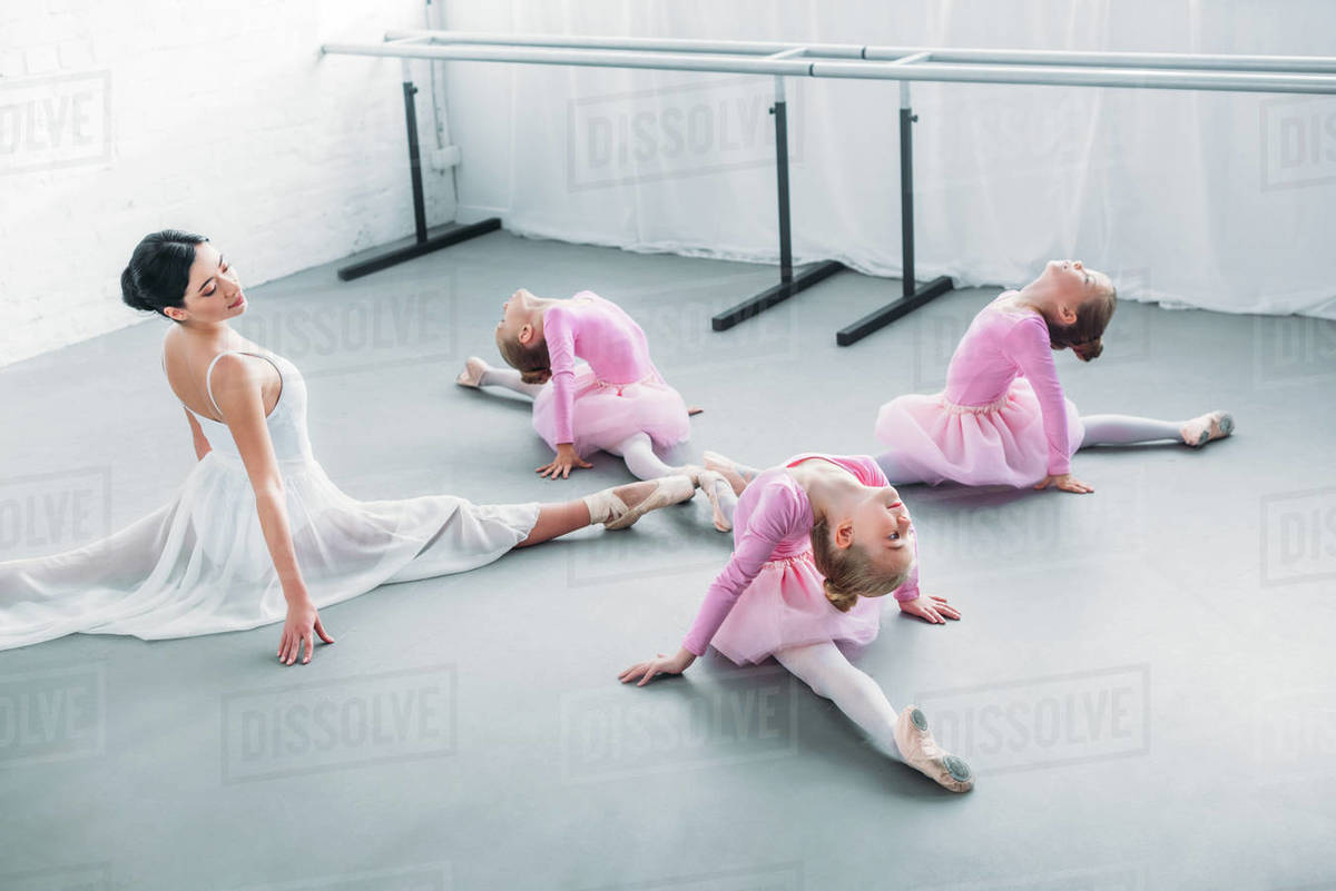 Adorable little ballerinas and young teacher stretching and exercising ...