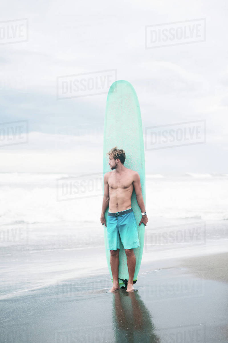 Shirtless surfer standing with surfboard in Bali, Indonesia - Stock ...
