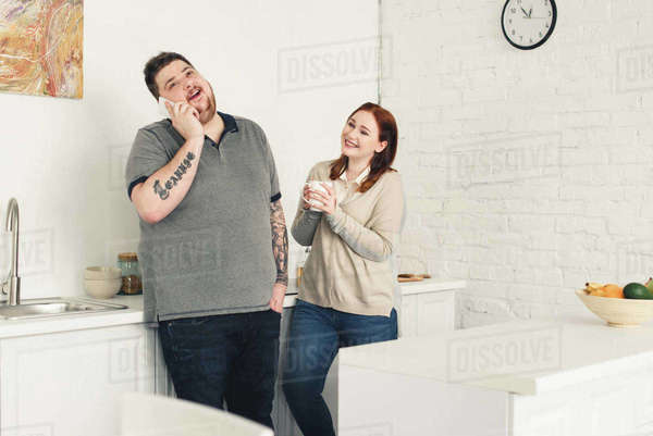 Happy boyfriend talking by smartphone and girlfriend holding cup of ...