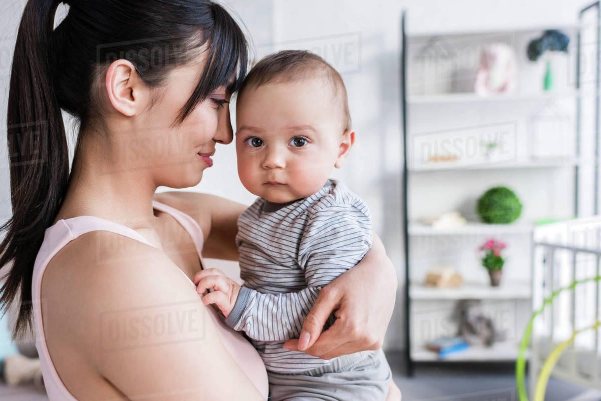Close-up portrait of young mother embracing her little child at home ...
