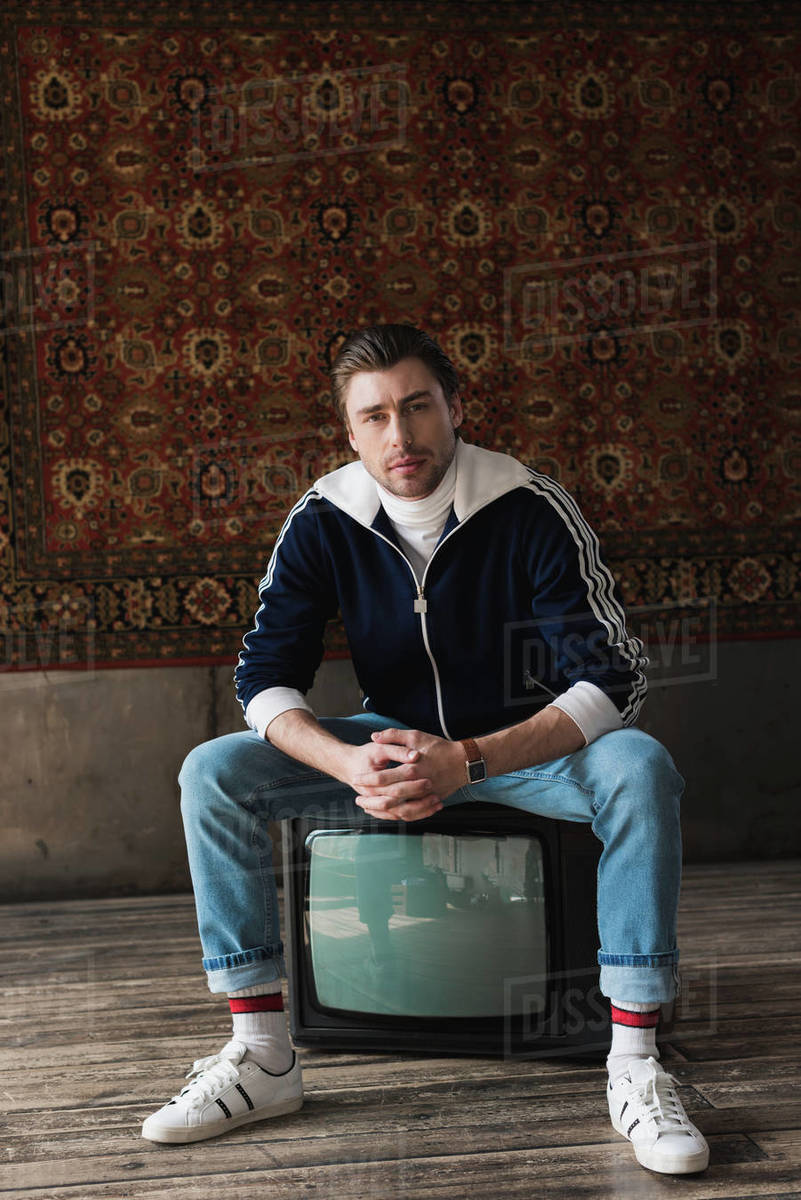 Handsome young man in vintage clothes sitting on retro tv set and ...