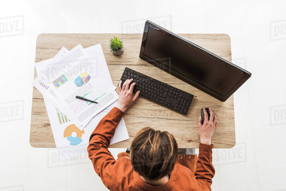 Top view of man working on computer at table with infographics and ...