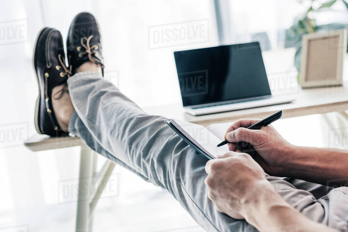 Cropped image of man writing in textbook and holding legs on table with ...
