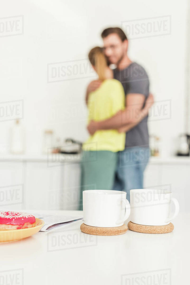 Close-up shot of two coffee cups at table with donuts and couple ...