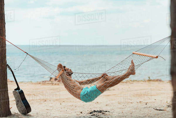 Handsome bearded man lying in hammock on beach near the sea - Royalty ...