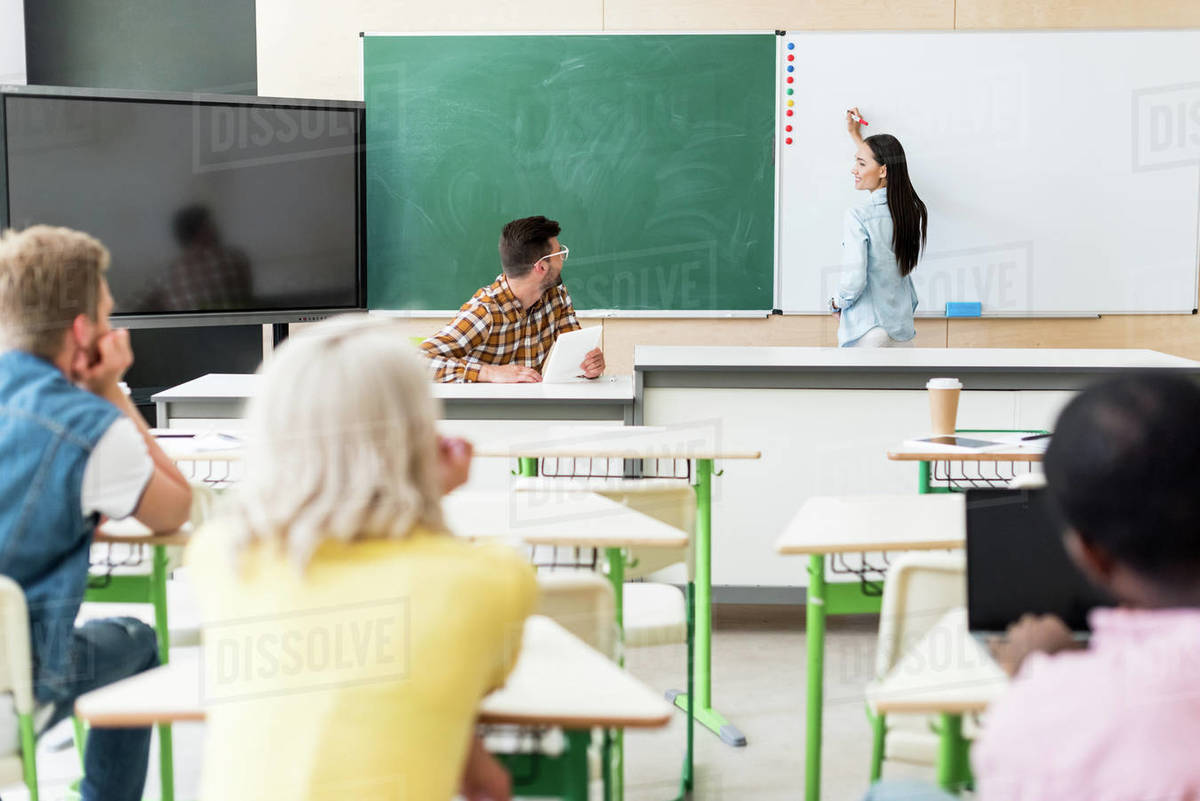 Rear view of young students sitting in classroom during lesson ...