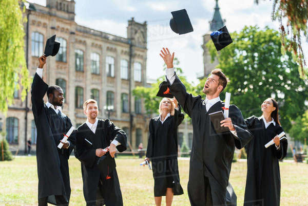 Young happy graduated students throwing up graduation caps in ...