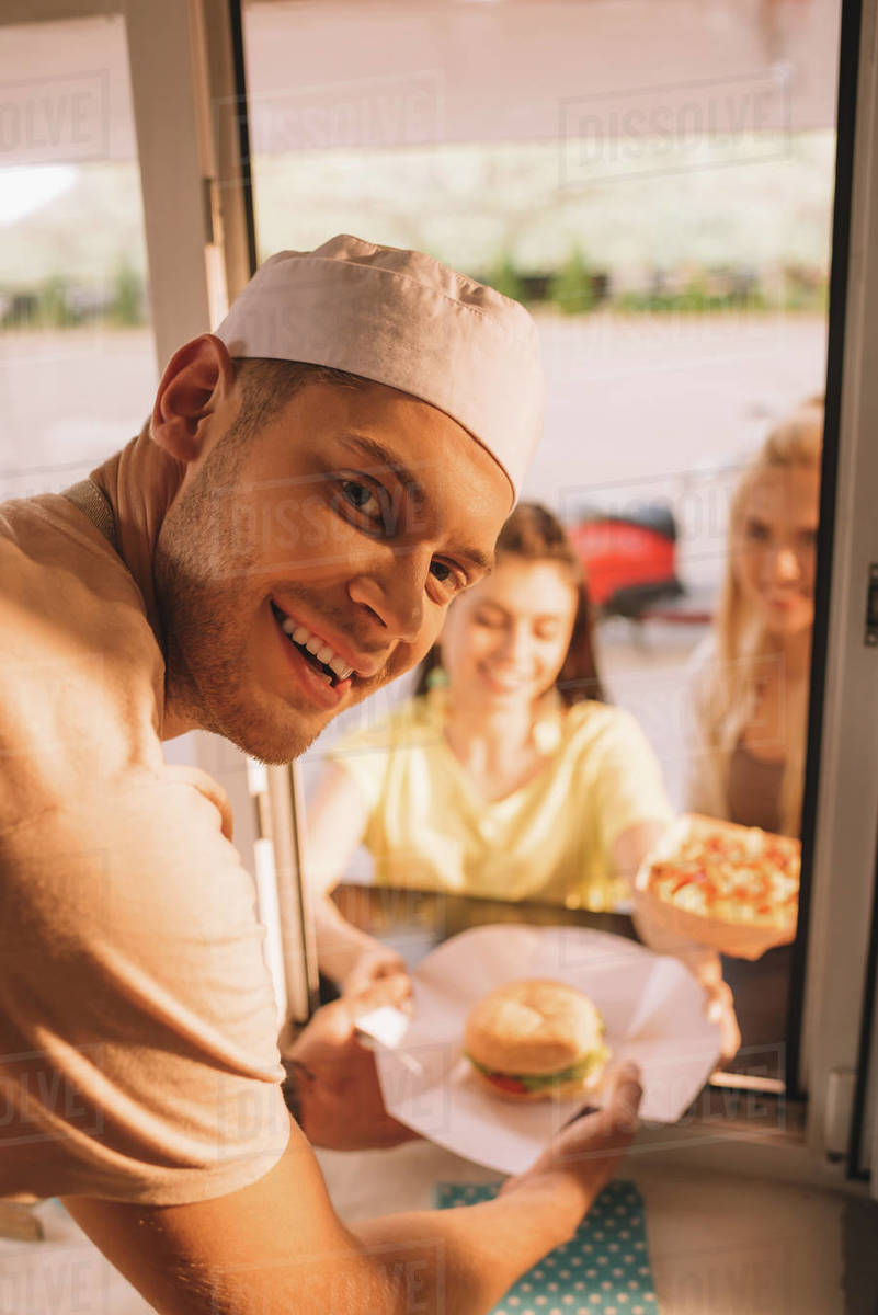 Smiling chef giving burger and french fries to customers from food ...