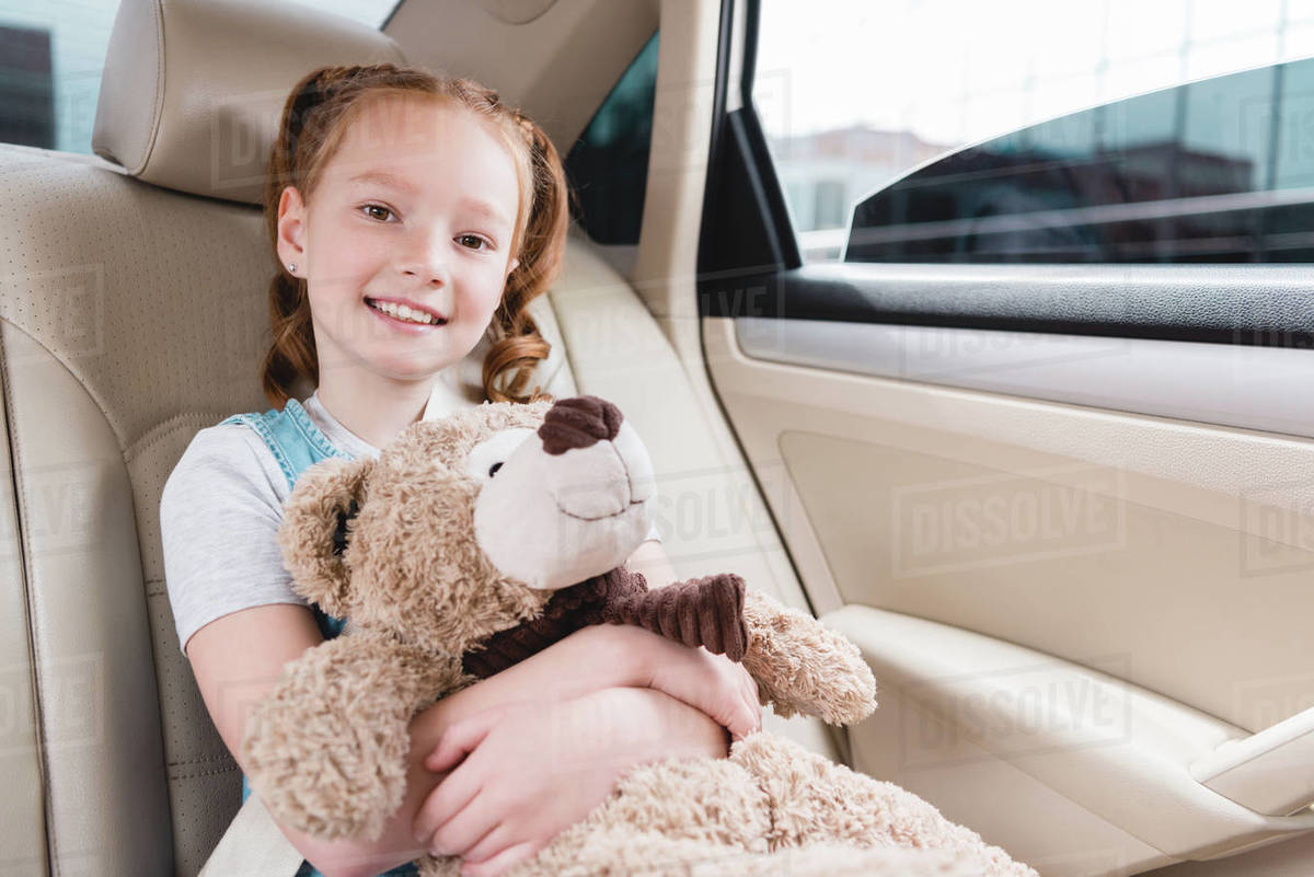 Portrait of cheerful kid hugging teddy bear while sitting in car ...