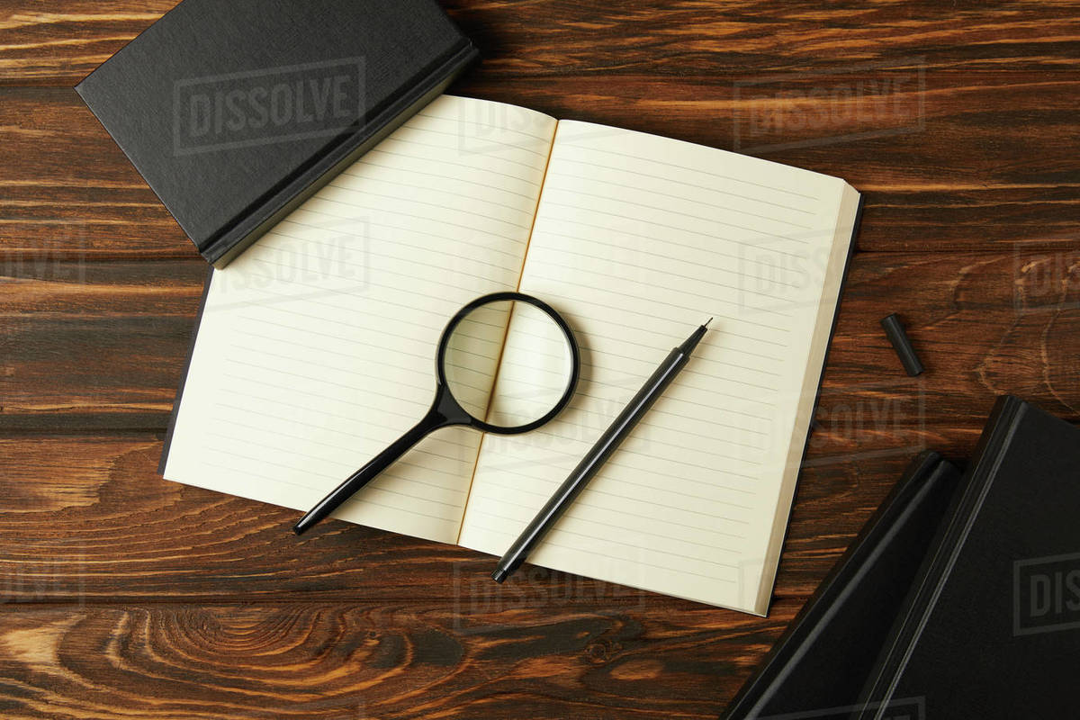 Top view of magnifying glass, notebooks and pen on wooden table - Stock ...