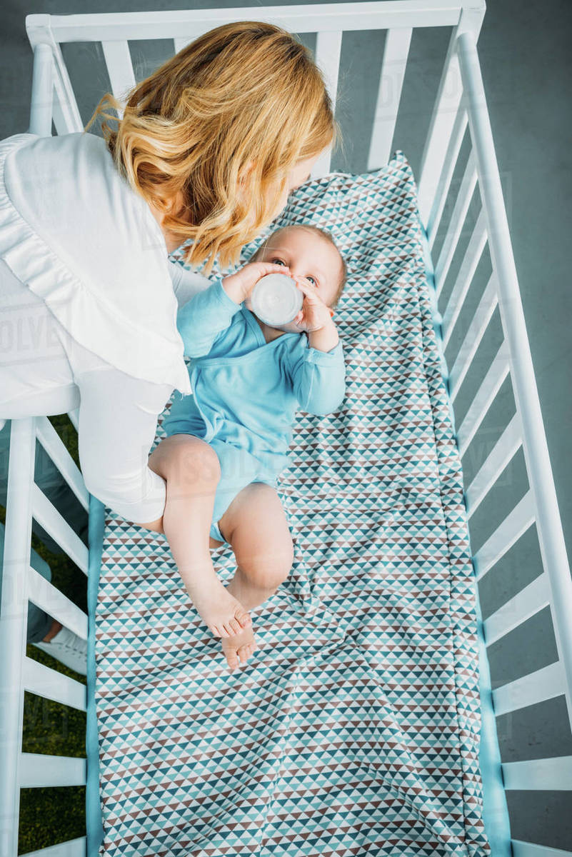 High angle view of mother putting her little child into crib at home ...