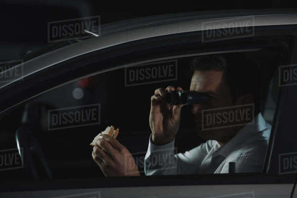 Male private detective doing surveillance by binoculars and eating ...