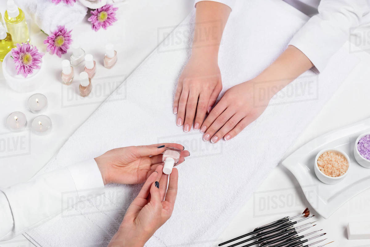 Cropped image of manicurist showing nail polish to woman at table with ...