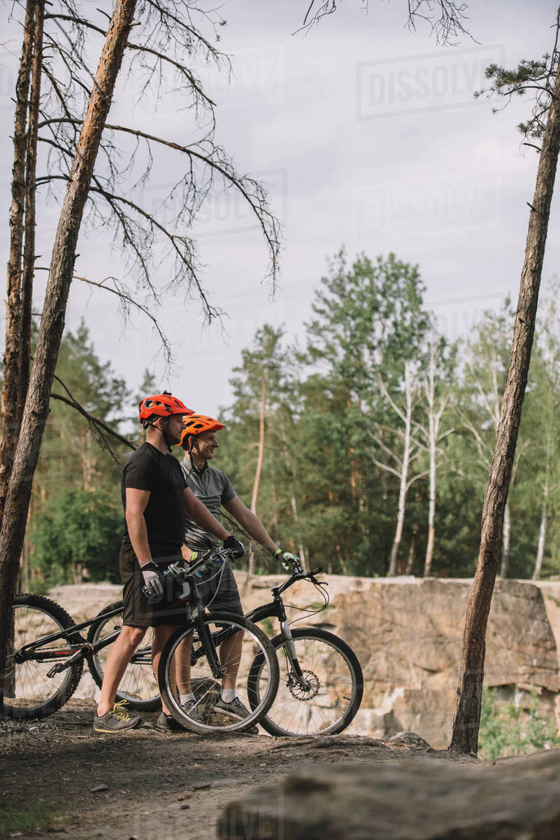 Handsome young trial bikers standing on cliff with bicycles - Royalty ...