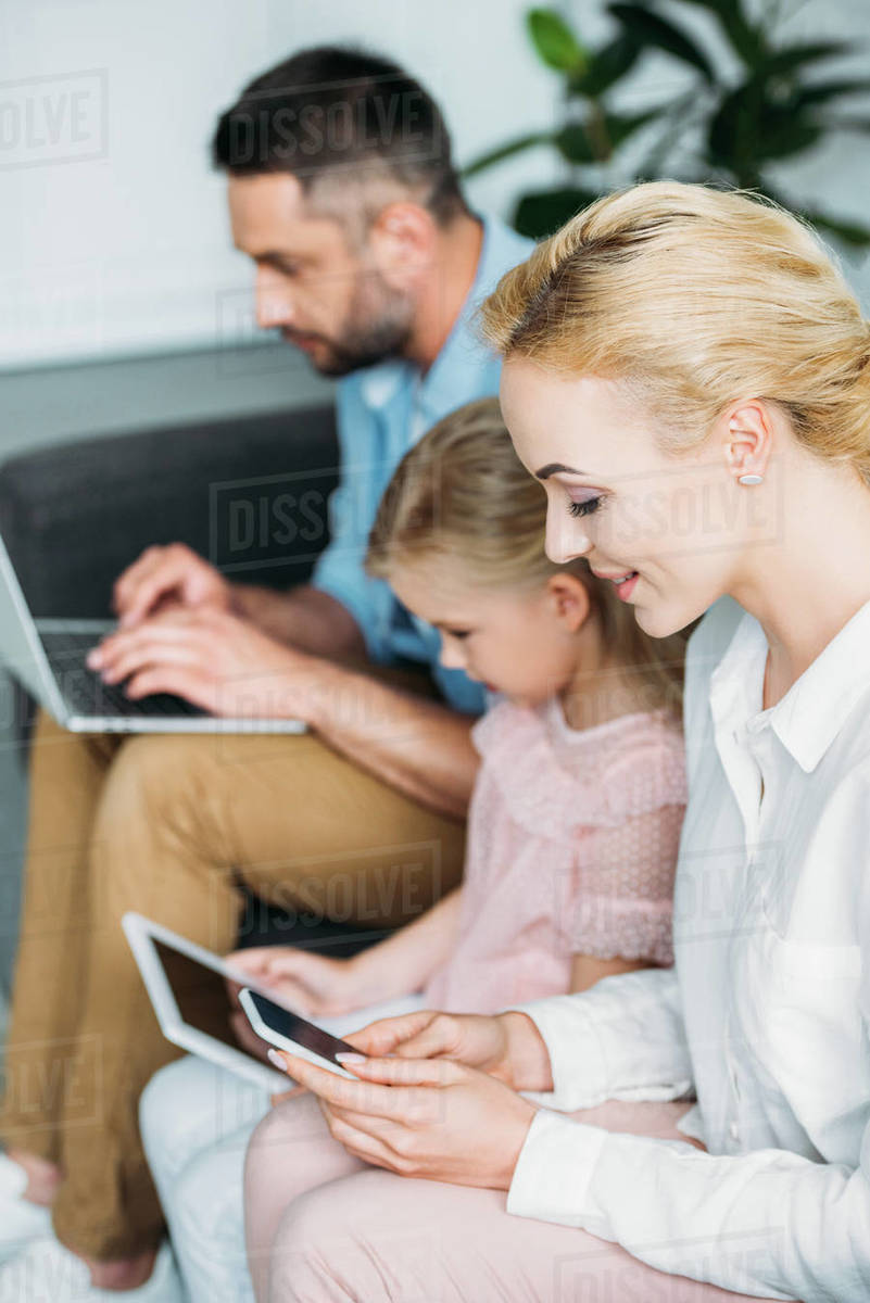 Family with one child using gadgets while sitting together at home ...