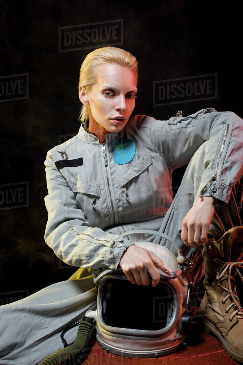 Attractive female astronaut in spacesuit holding helmet and sitting on ...