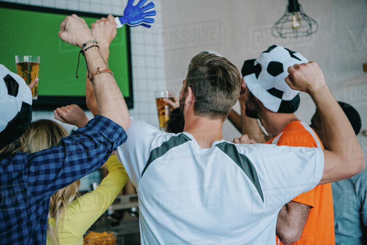 Rear view of football fans in soccer ball hats celebrating with hand ...