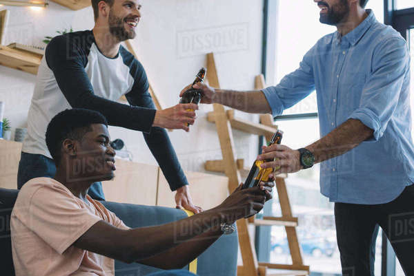Cropped shot of man giving beer bottles to smiling multiethnic friends ...