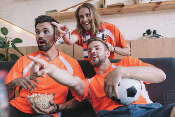 Young male football fans in orange t-shirts pointing by fingers to ...