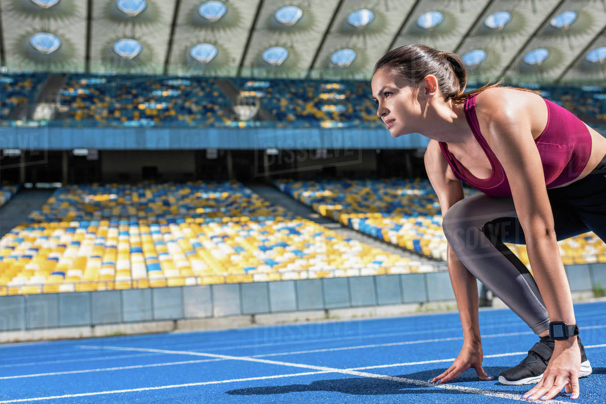 Athletic female runner in start position on running track at sports ...