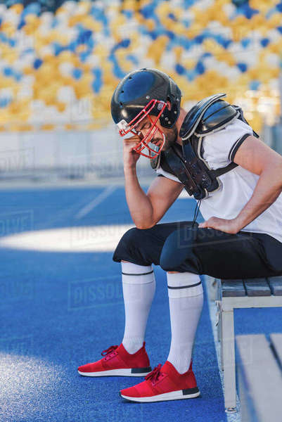 Depressed young american football player sitting at sports stadium ...