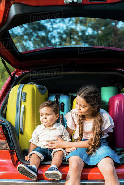 Brother and sister sitting near travel bags in car trunk - Royalty-free ...