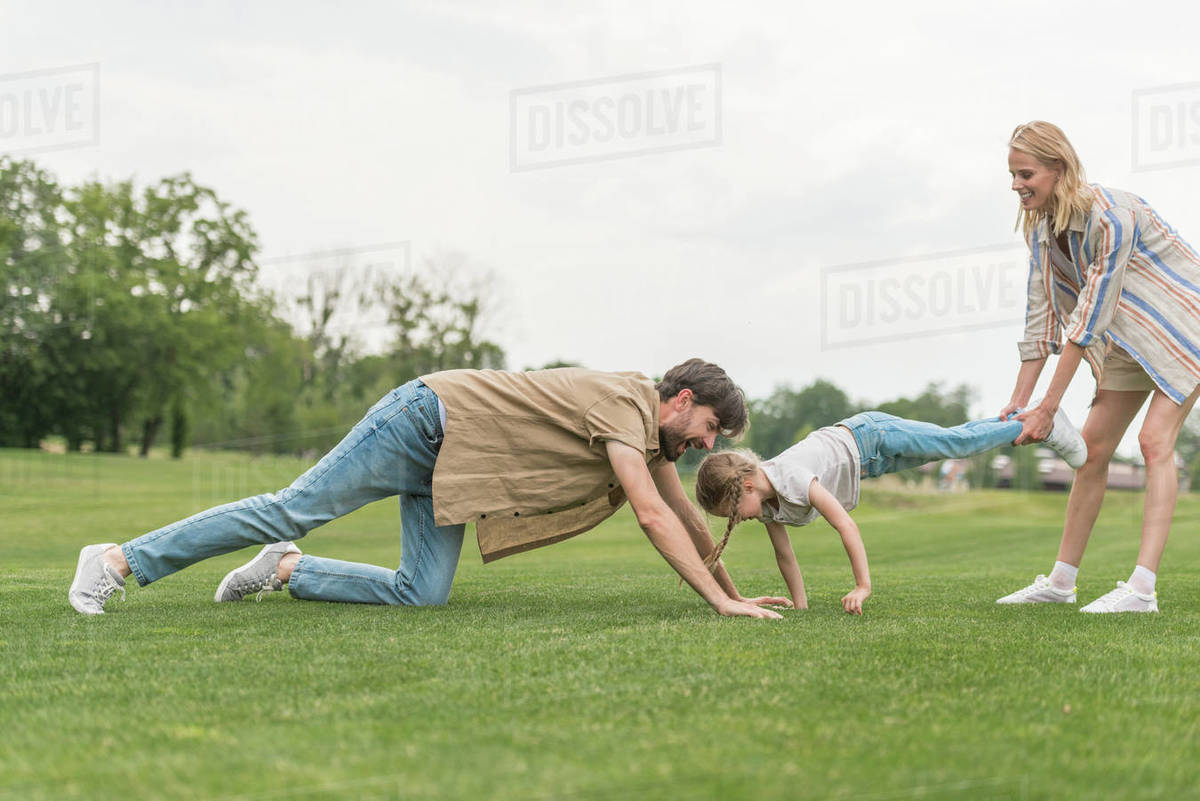Side view of happy family having fun on green grass in park - Royalty ...