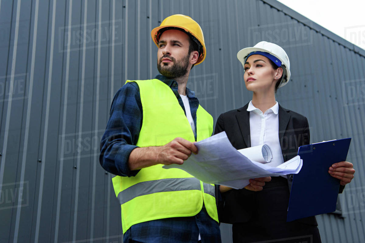 female engineer and male worker with blueprints and clipboard looking ...