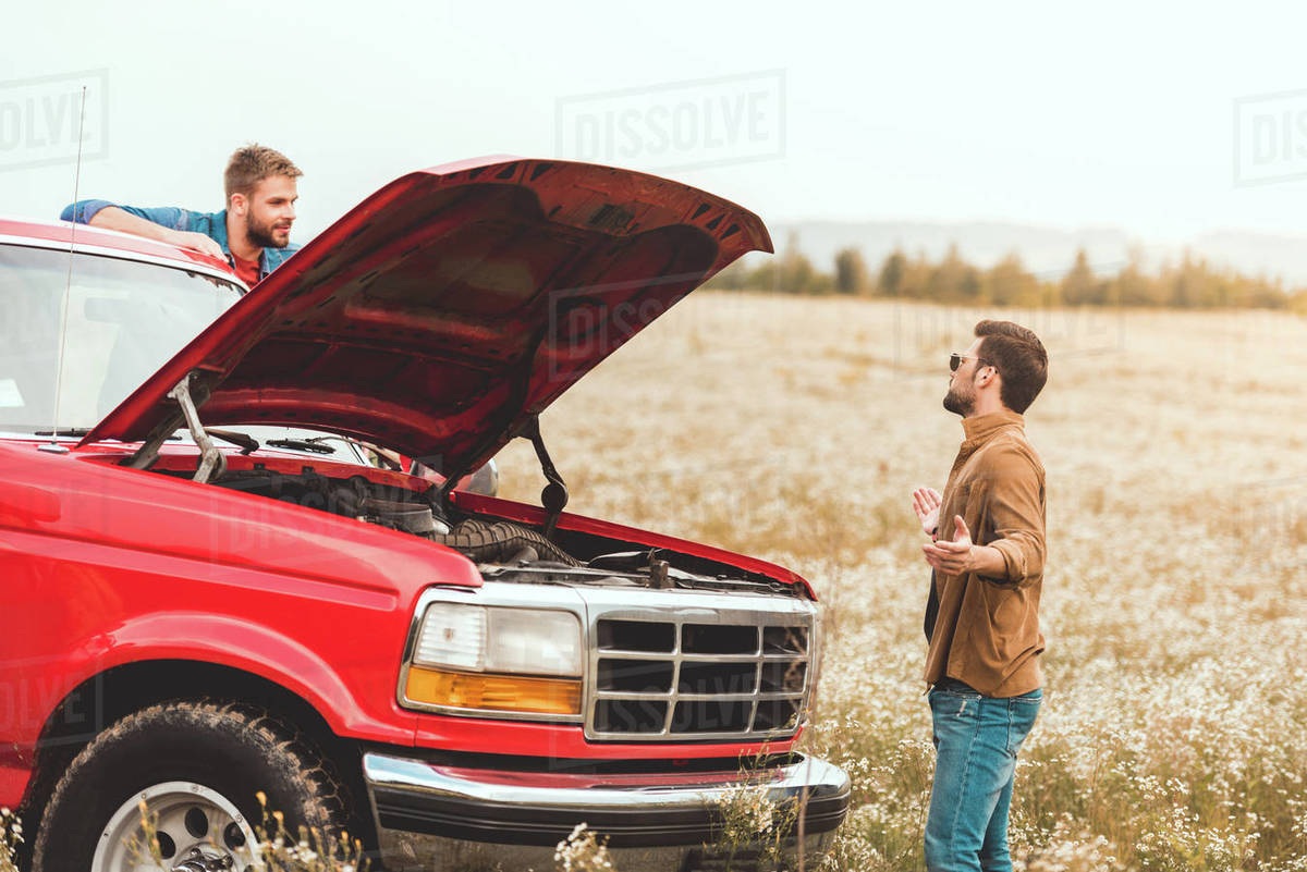 young men standing near car with broken engine in field - Royalty-free ...
