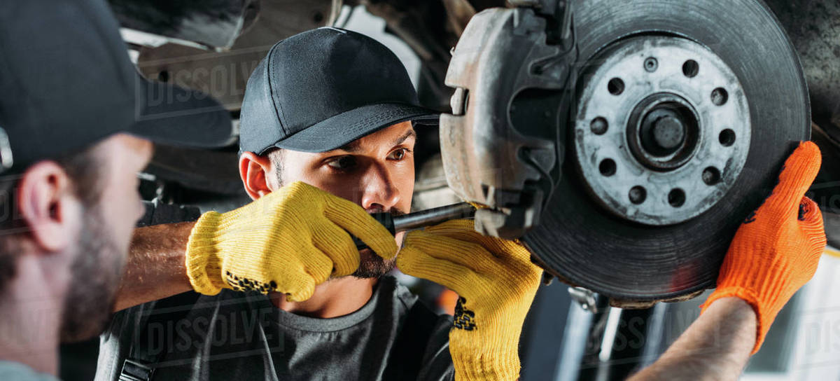 Professional mechanics repairing car without wheel in workshop ...