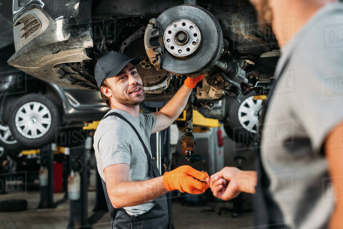 Professional manual workers repairing car without wheel in mechanic ...
