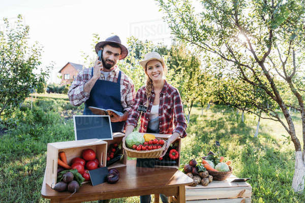 two smiling farmers selling organic locally grown vegetables at market ...