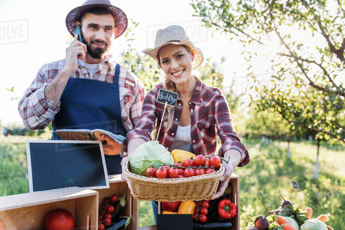 two smiling farmers selling fresh organic vegetables at market ...