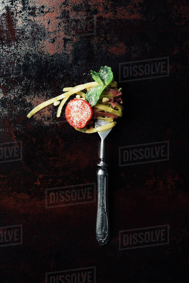 top view of fork wrapped by pasta with mint leaves, jamon and cherry ...