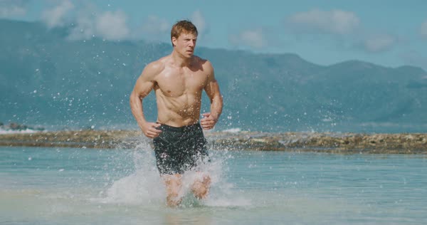 Young attractive muscular man running on the beach in slow motion ...