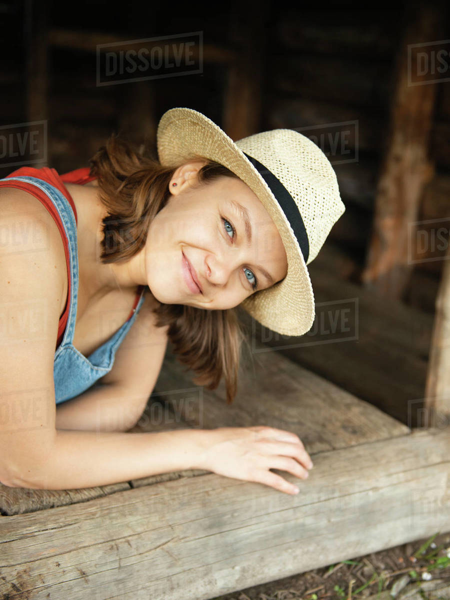 Portrait of a smiling woman in a straw hat looking out from window ...