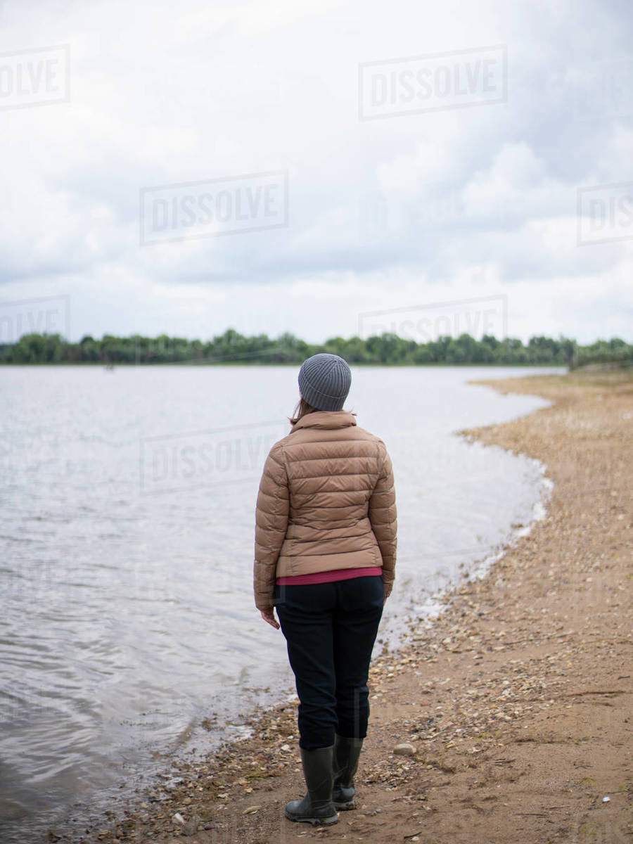 Back view of woman standing at river bank looking at water - Stock ...