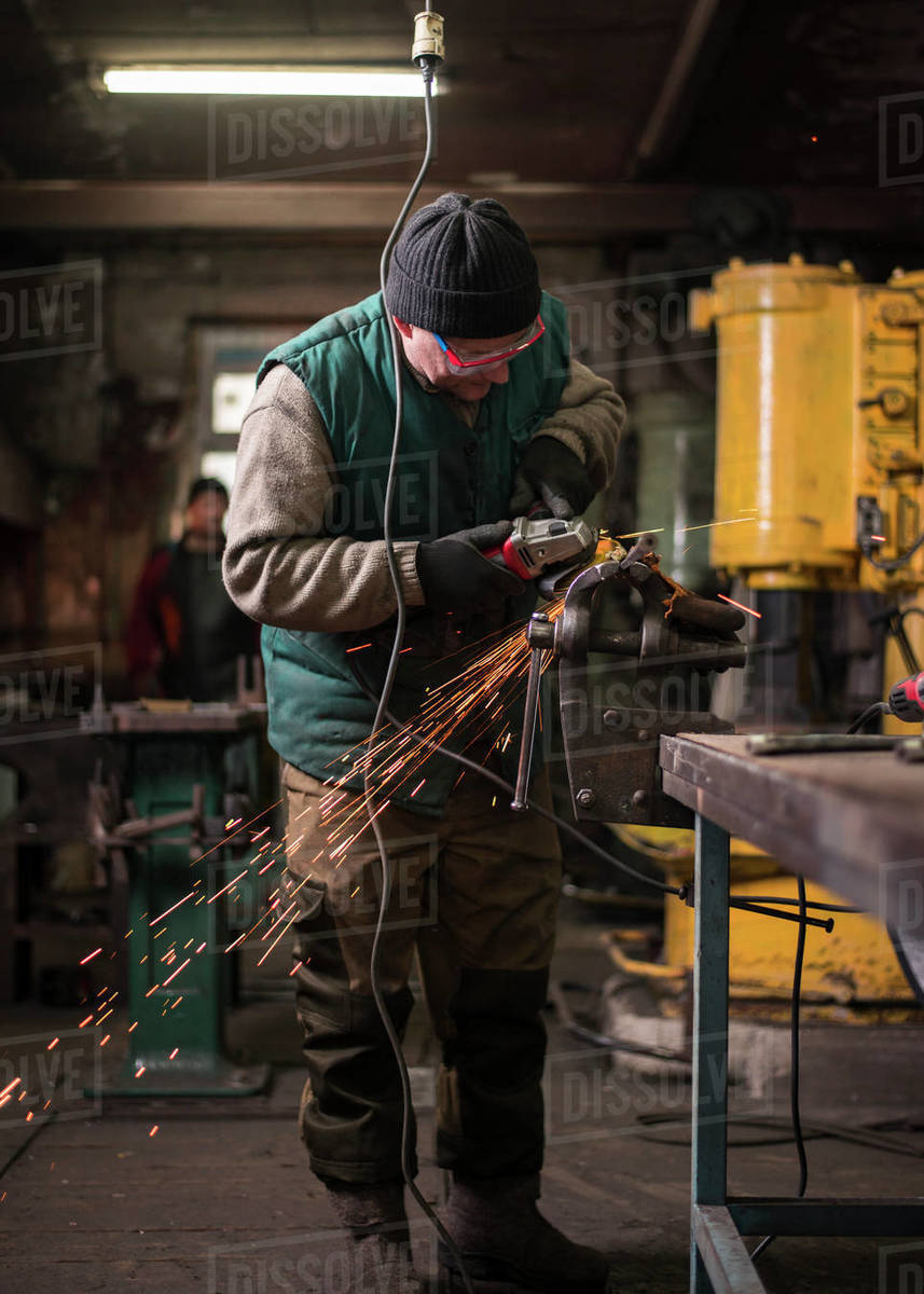 Blacksmith standing and sawing iron piece in his workshop - Stock Photo ...
